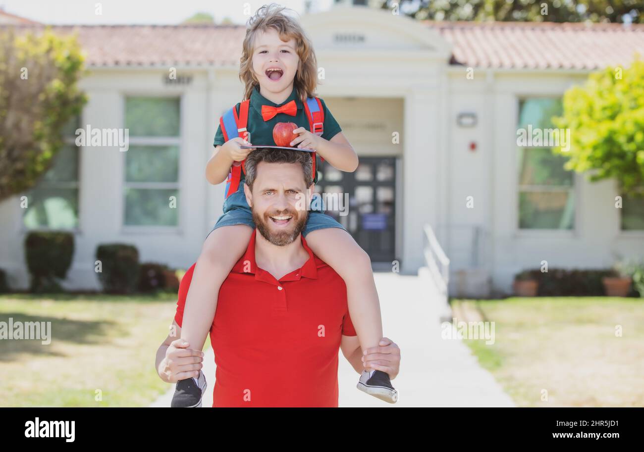 Parent and amazed child piggyback near school. School boy going to ...