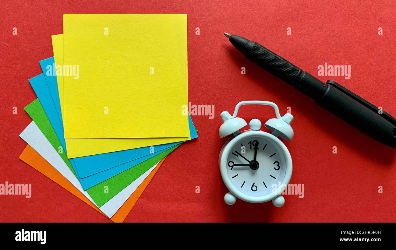 Top view of white alarm clock, notepads and pen on red background. Copy ...