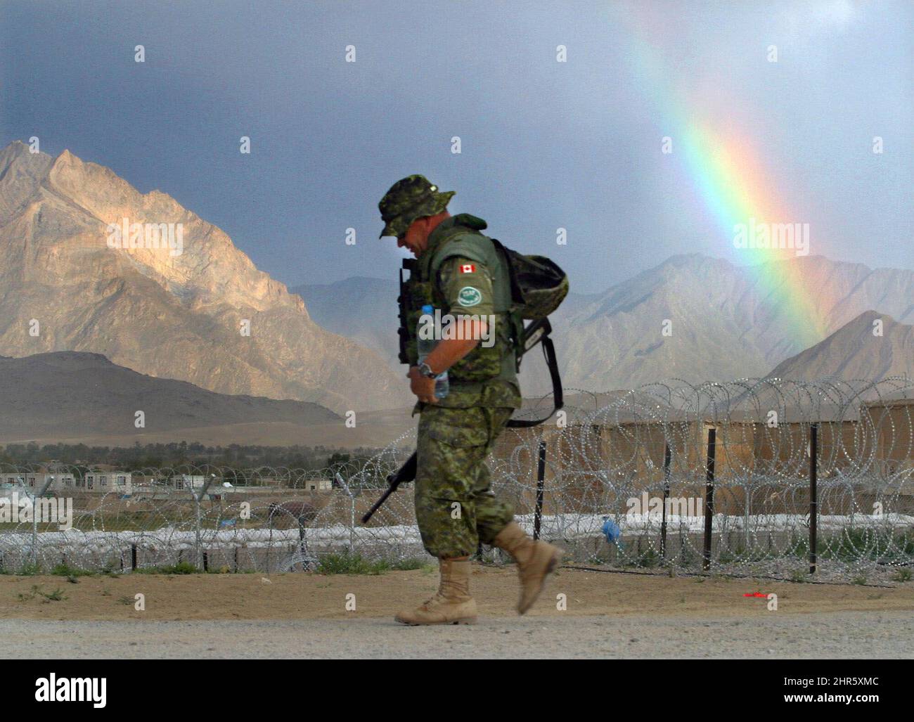 A Canadian 3RCR Battlegroup soldier walks past an evening rainbow in ...