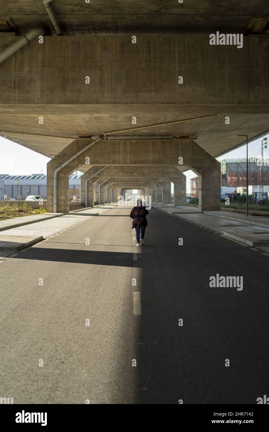 Vertical back view of a female walking on a road under a stone bridge ...