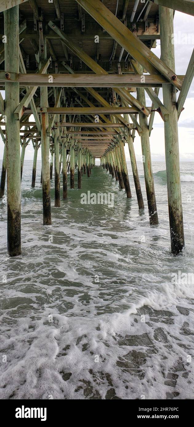 View of waves and wooden beams support under the pier at the beach ...