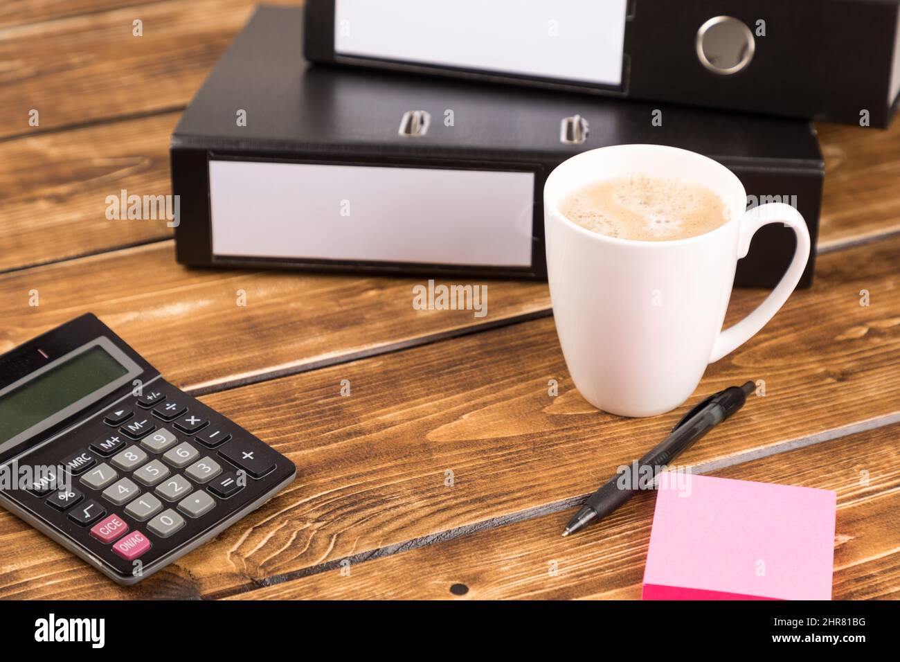 Cup of coffee, folder, calculator, pen, and a sticky note on a wooden ...
