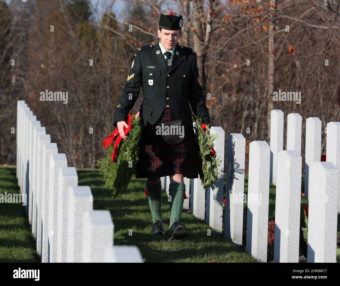 A Canadian Army member carries a pair of wreaths to headstones of ...