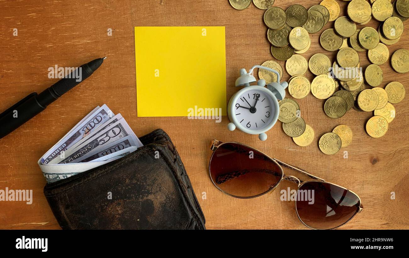 Top view of wallet, bank notes, coins, alarm clock, glasses and pen on ...