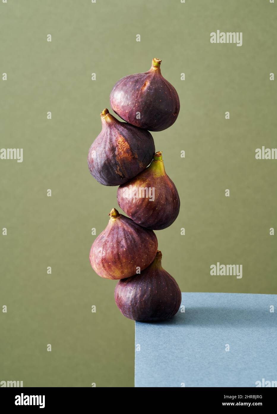 Fresh figs balancing on the edge of a table, with green background ...