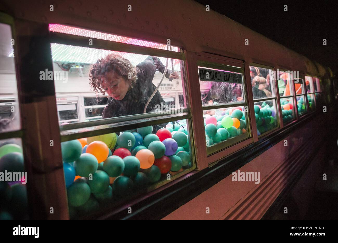 A young boy plays in a school bus filled with plastic ball pit balls ...
