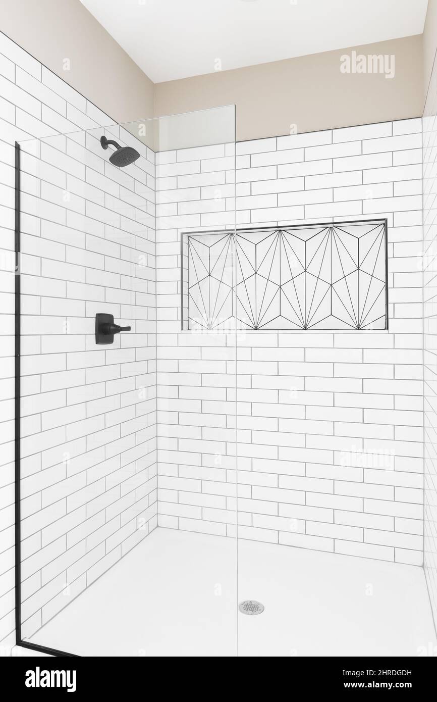 A renovated shower with white subway tiles, glass wall, black faucet ...
