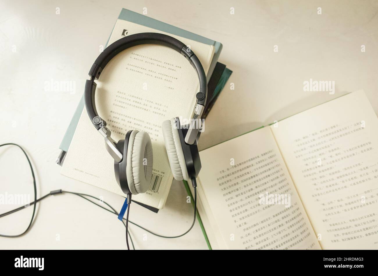 Top view of a pair of headphones on a pile of books with an opened one ...