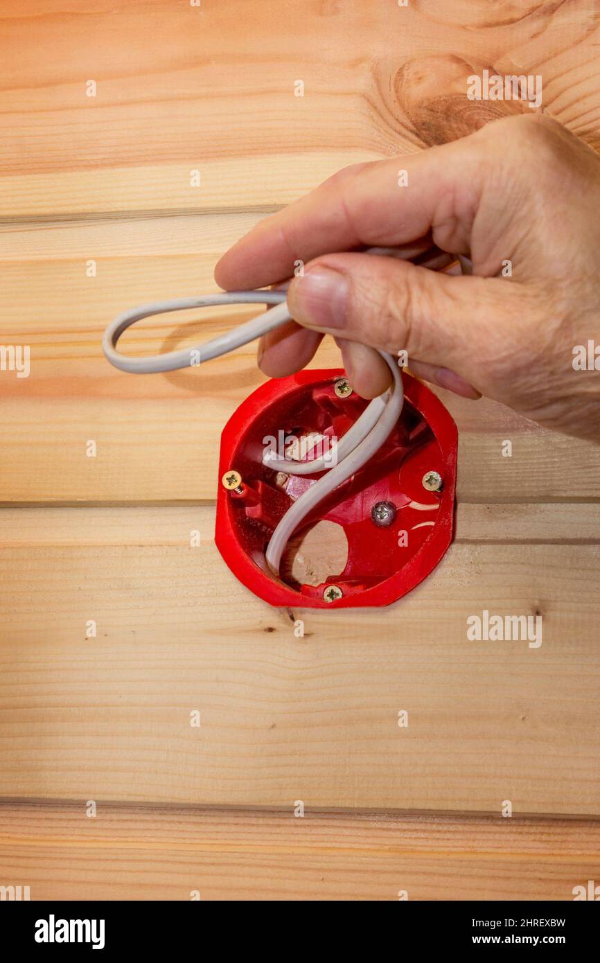 An electrician installs an indoor outlet into a wall sheathed with ...