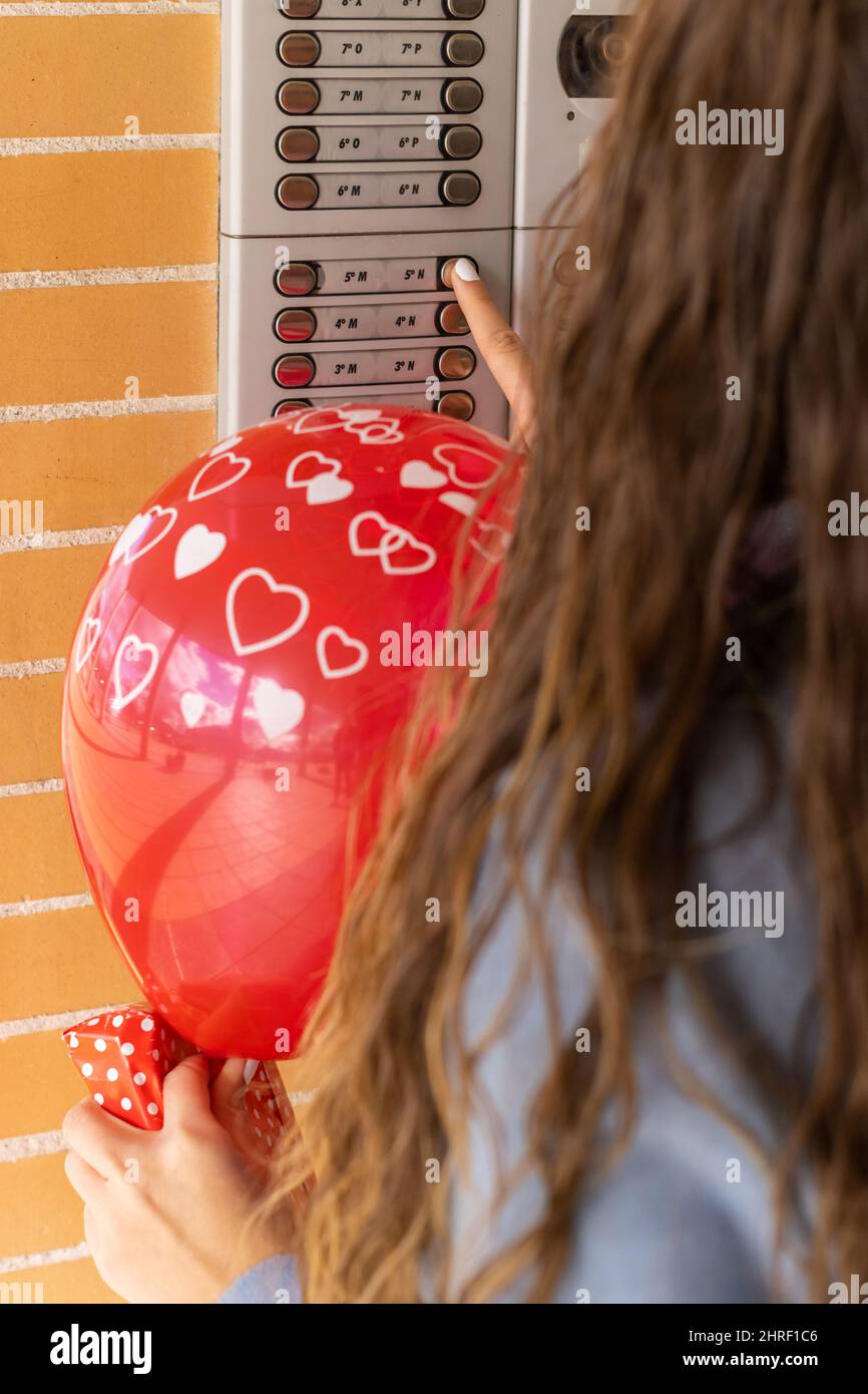 Vertical of a Caucasian girl pressing the doorbell, holding a balloon ...