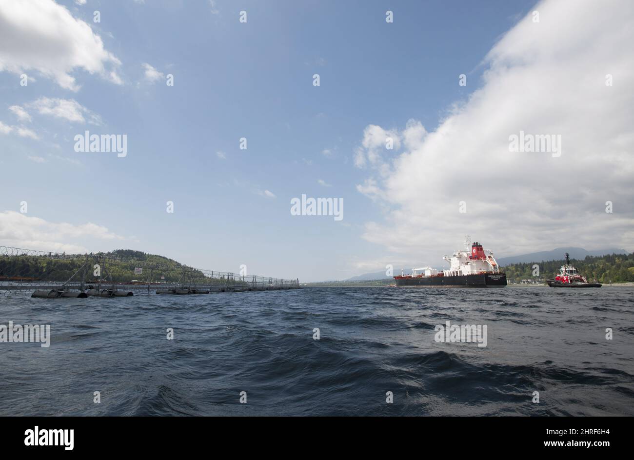 A oil tanker passes a floating chain link fence topped with razor wire ...