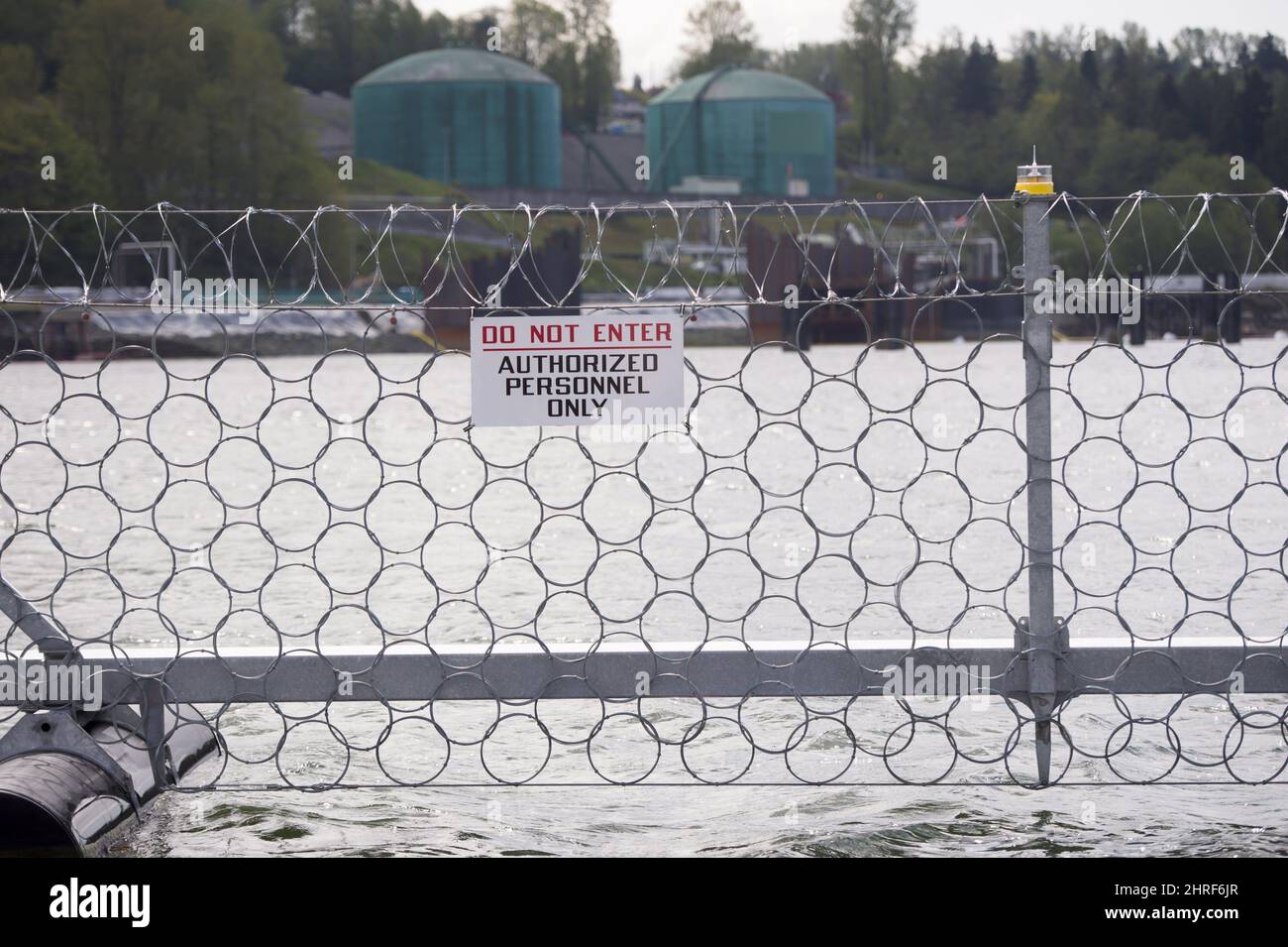 Oil tanks can be seen behind a floating chain link fence topped with ...