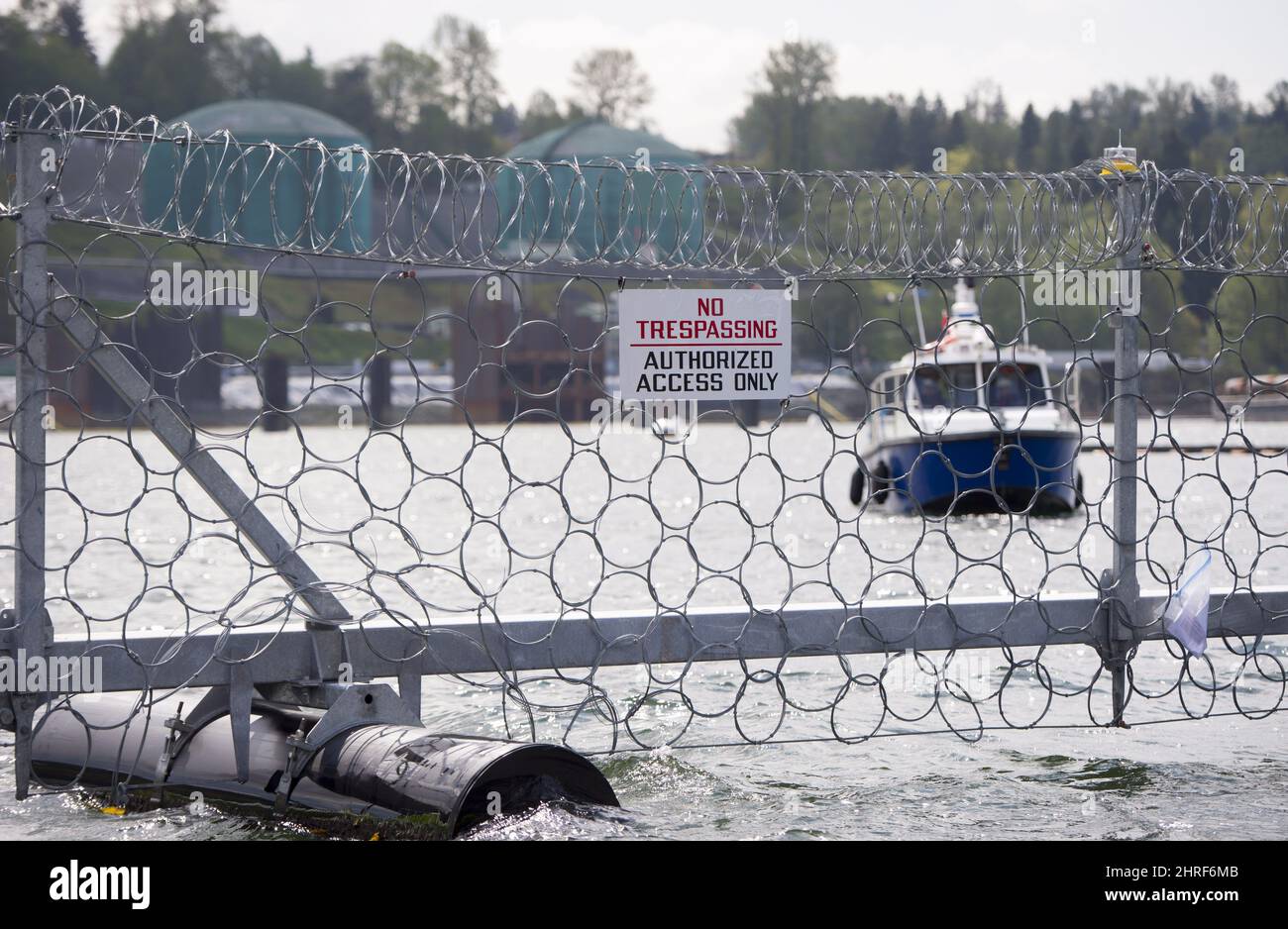 A patrol boat guards a floating chain link fence topped with razor wire ...