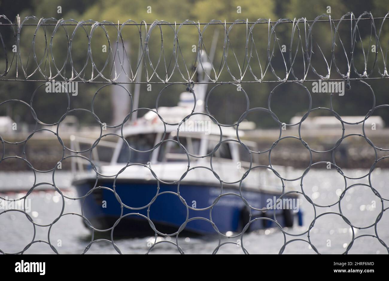 A patrol boat guards a floating chain link fence topped with razor wire ...