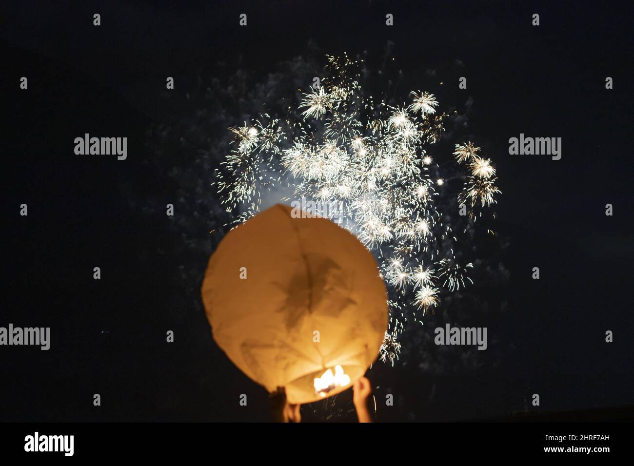 A paper sky lantern against a night sky with fireworks Stock Photo - Alamy