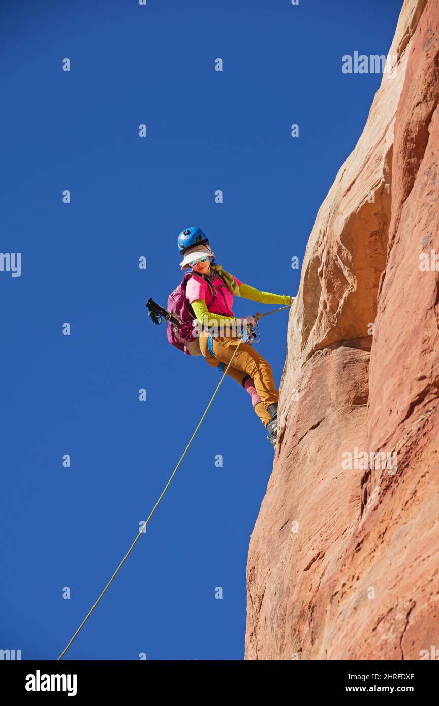 woman with pink shirt and blue helmet rappelling down a red sandstone ...