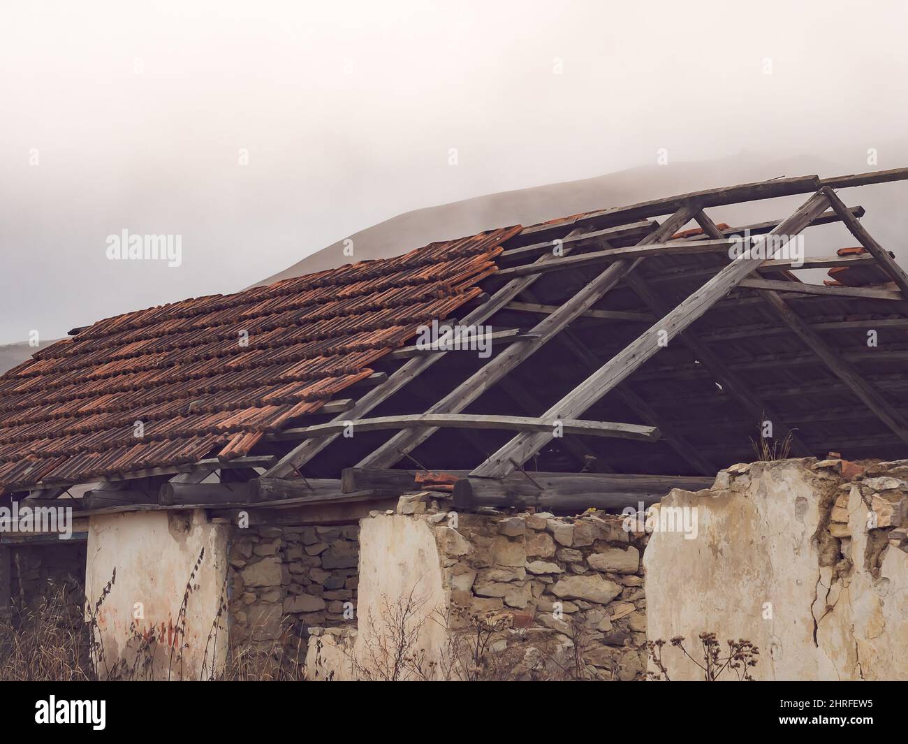 Roof and walls of ruined old house with mystical cloud haze descending ...