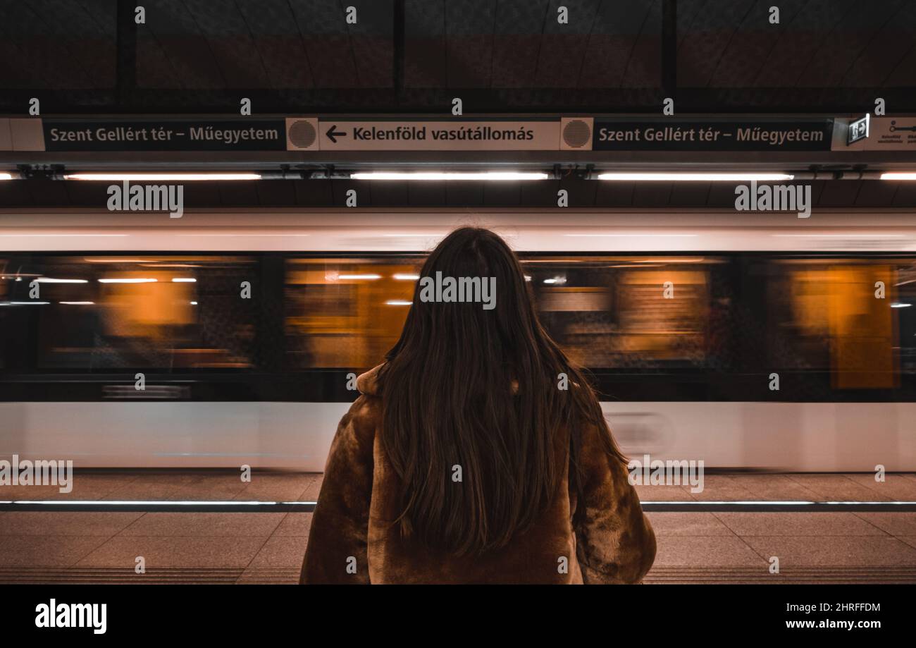 Female standing at the metro station with a long exposure of a train ...