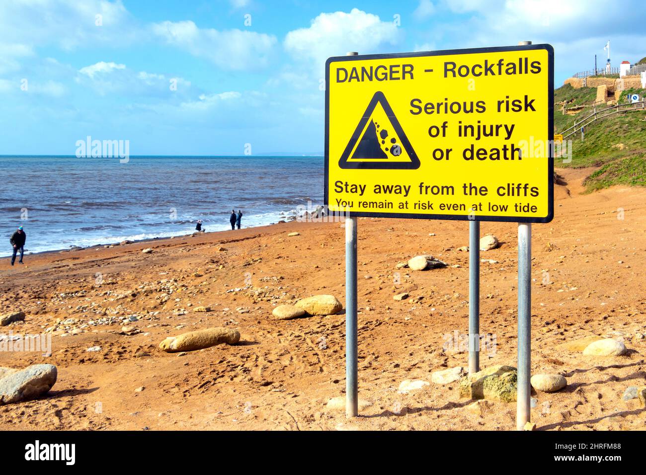 Yellow danger sign on beach warning of falling rocks and serious risk ...