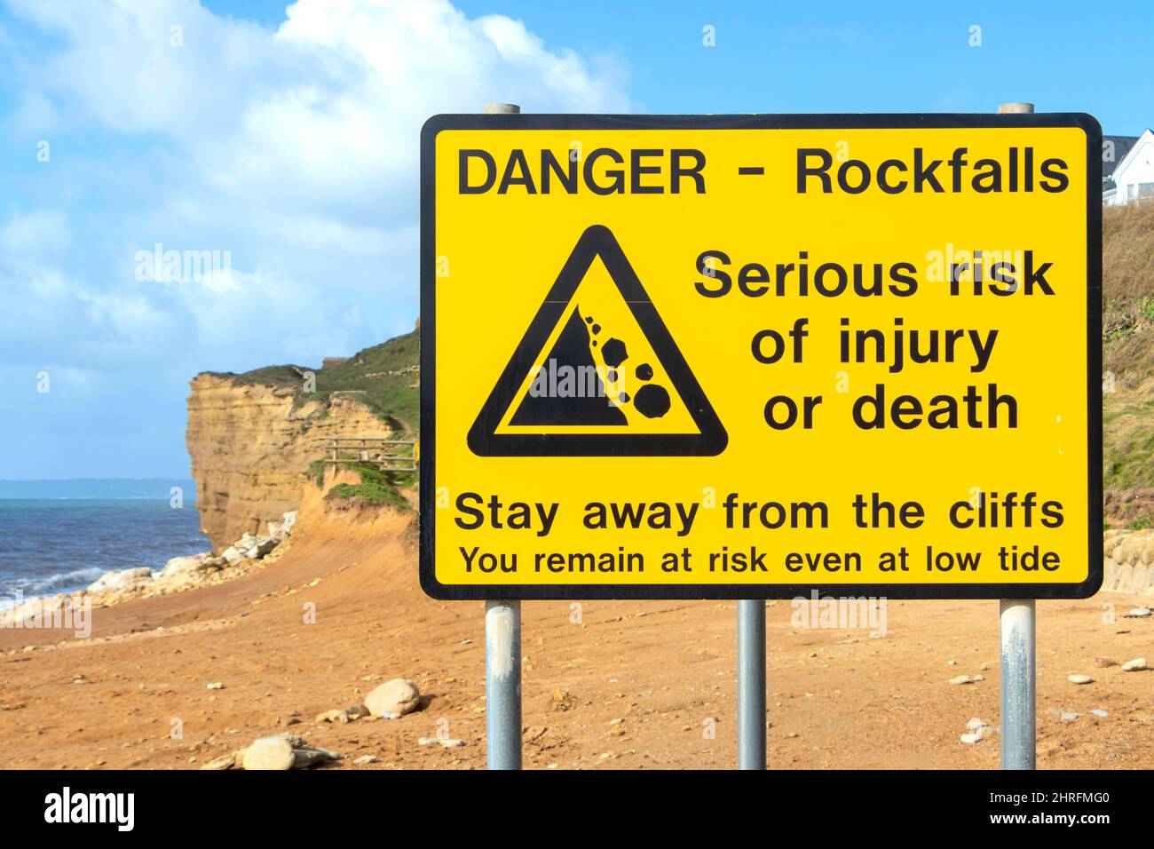 Yellow danger sign on beach warning of falling rocks and serious risk ...