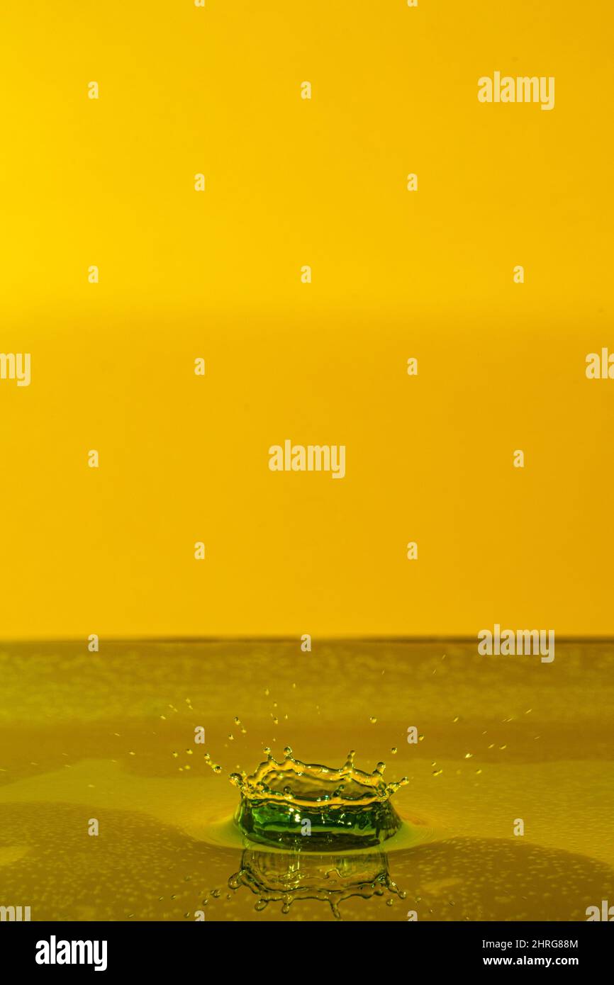 Vertical shot of a water splash in a studio on a yellow background ...