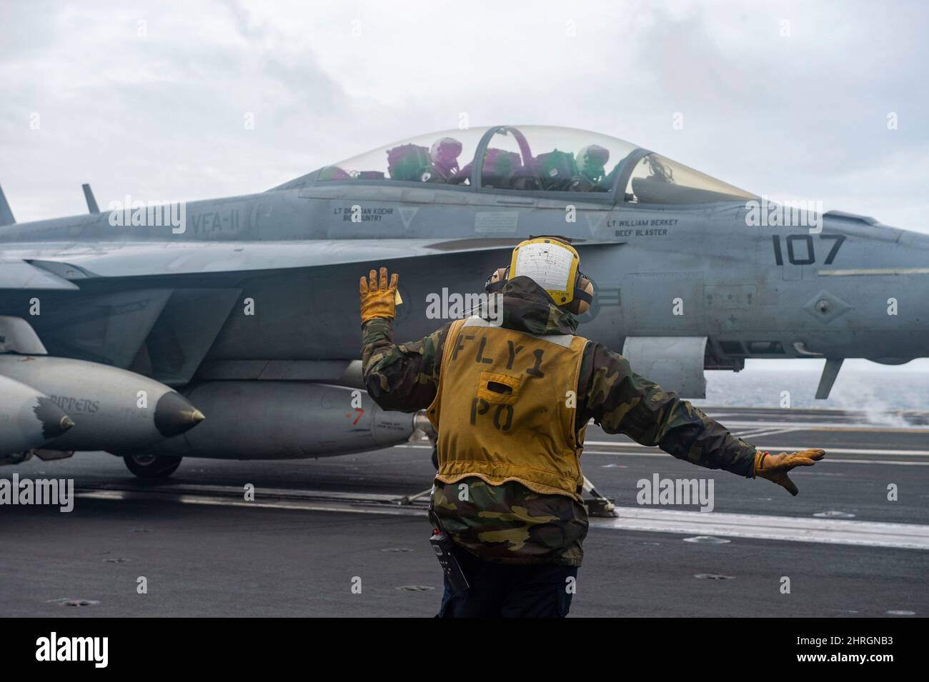 A U.S. Navy sailor directs the pilot of an F/A-18F Super Hornet fighter aircraft, attached to ...