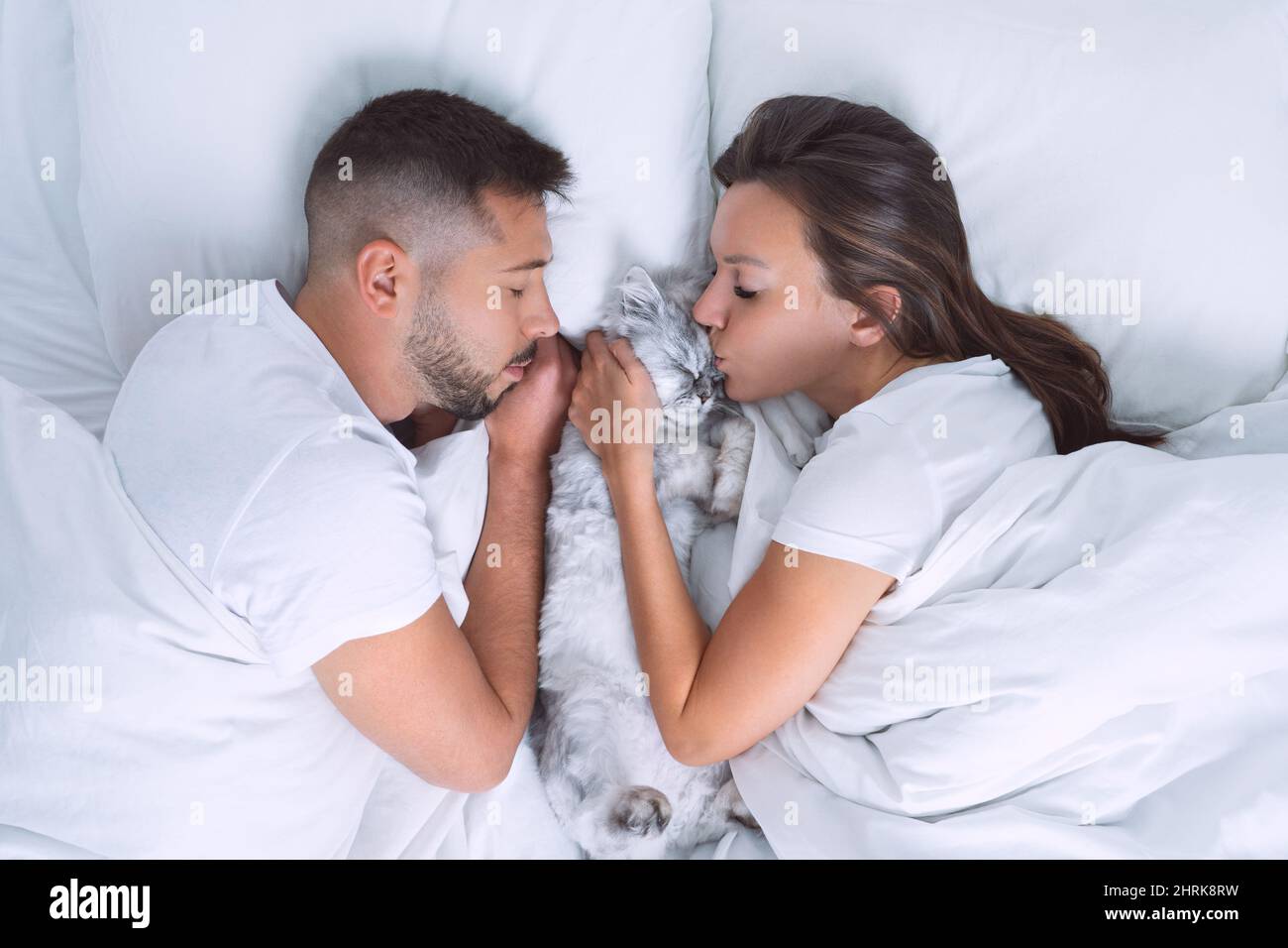 Beautiful couple lying on the bed with their lovely cat. Woman kissing ...