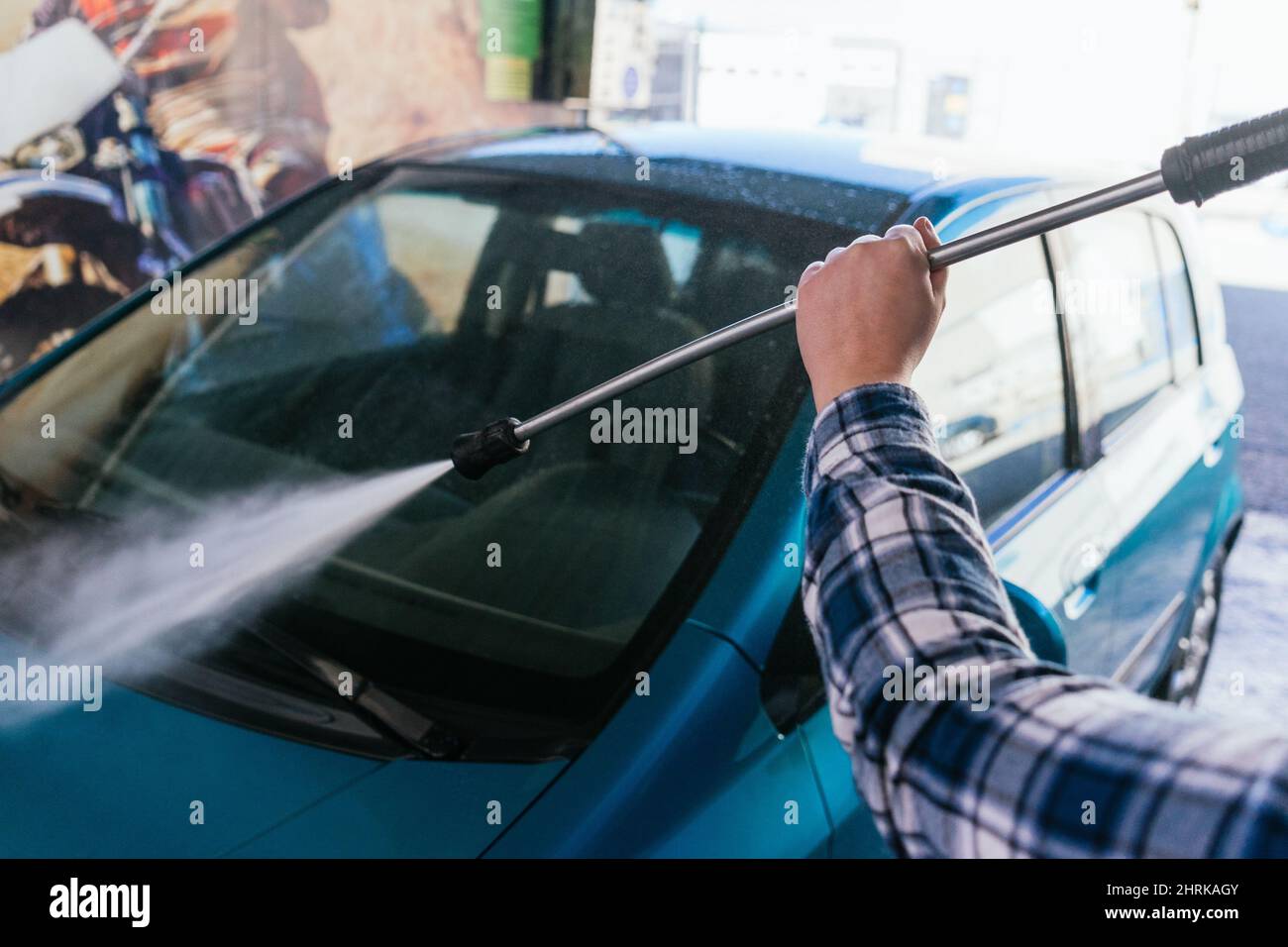 Detail of a young woman's arm washing the front of her car with a hose ...