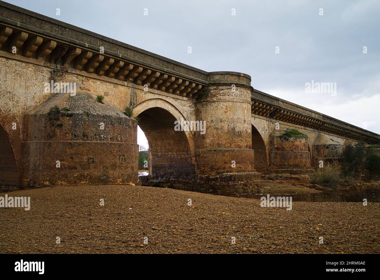 Old Roman bridge over a dried river under a cloudy sky on a gloomy day ...