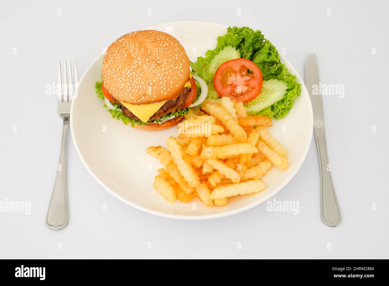 Serving of cheeseburger with French fries and vegetables on a white ...