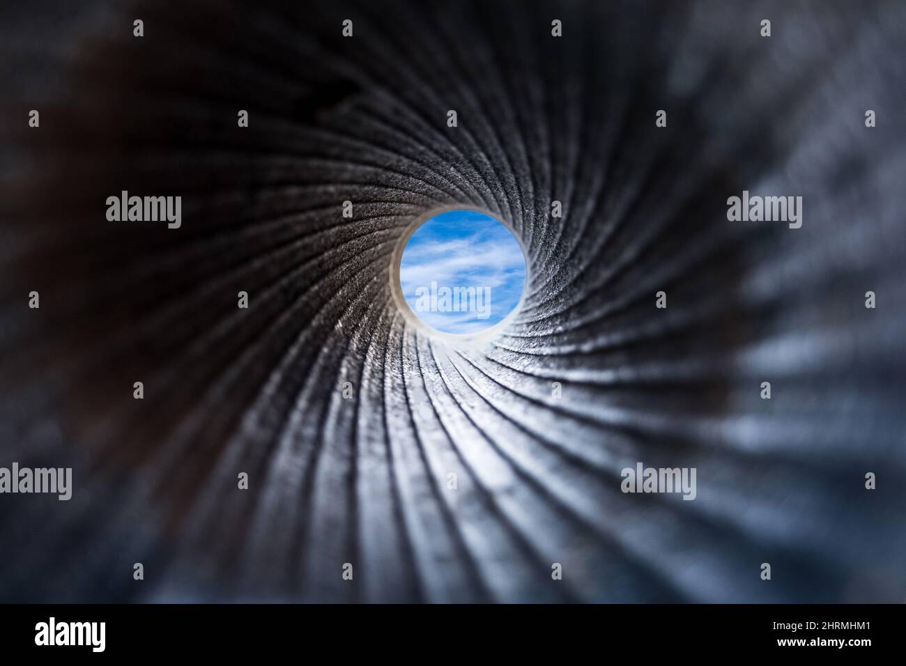 A view through a dark barrel of cannon to the blue sky with white ...
