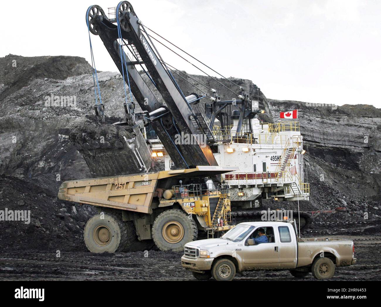A pickup truck passes a mining shovel filling a haul truck at an ...