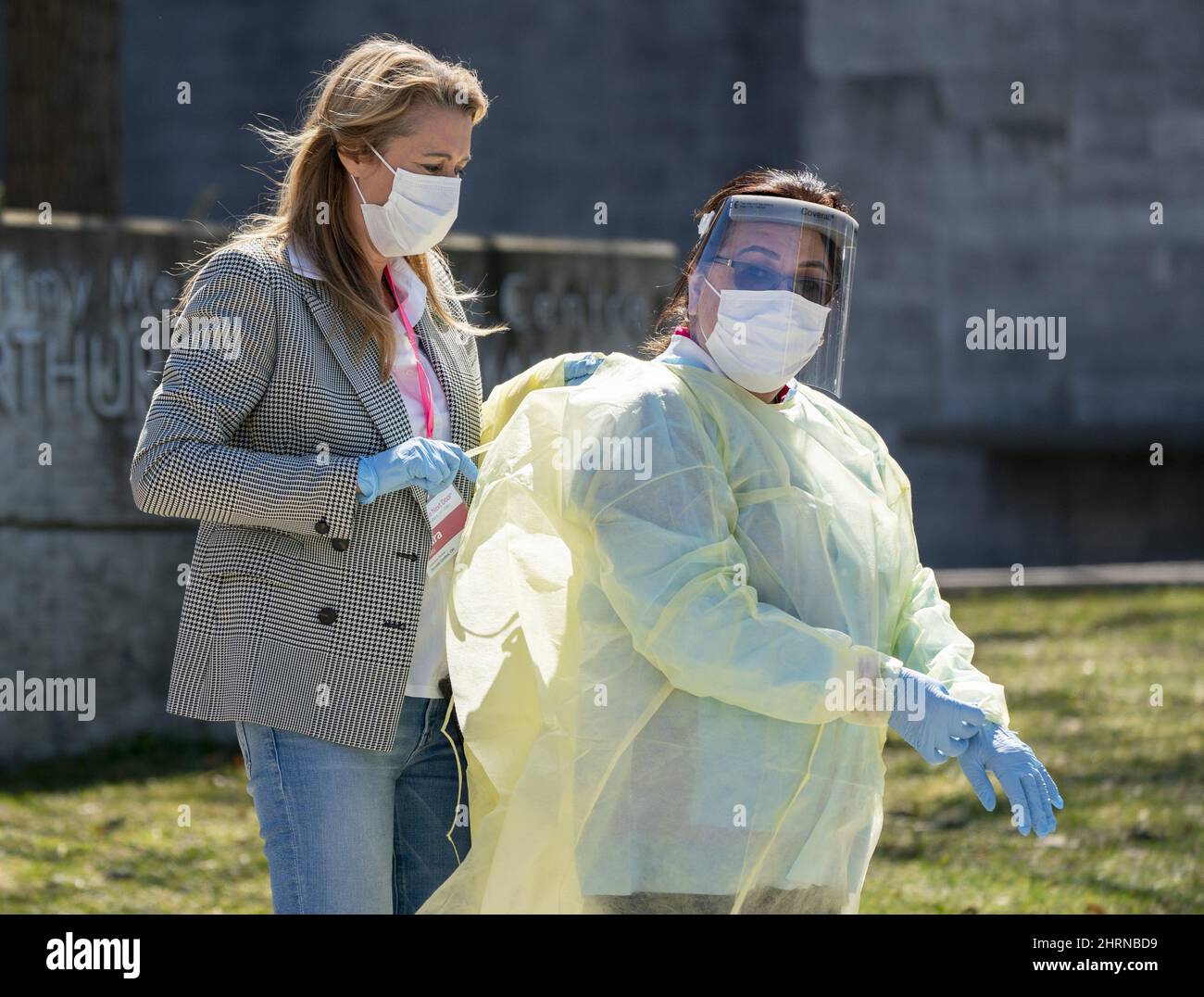 Two health care workers gown up on the sidewalk before going in to ...