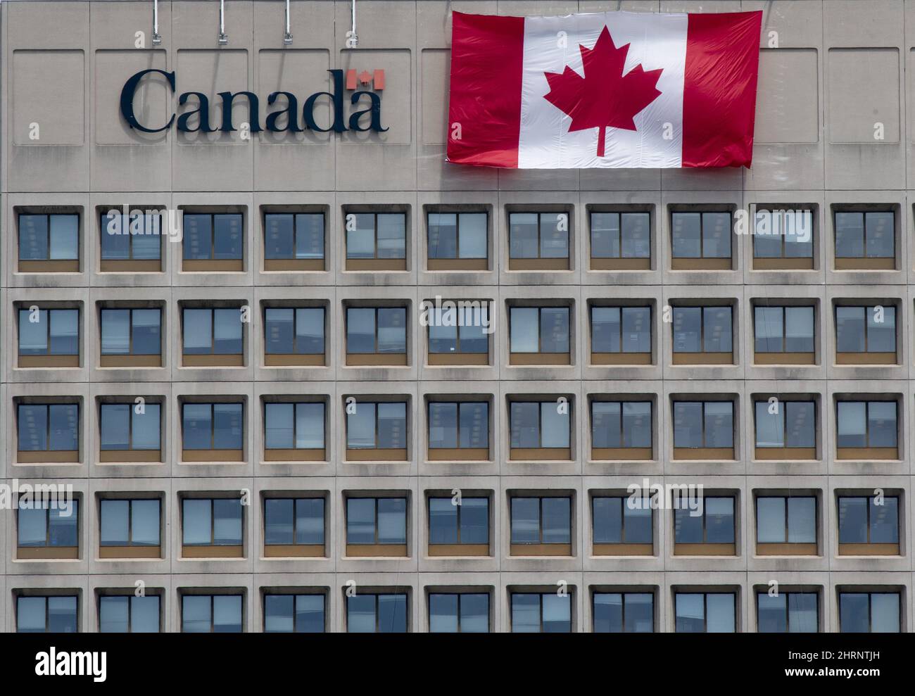 A giant Canadian flag hangs on the side of a government office building ...
