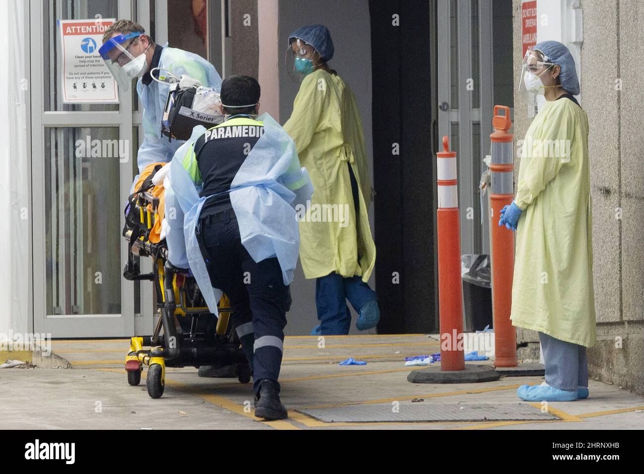 Paramedics wearing personal protective equipment wheel a patient into ...