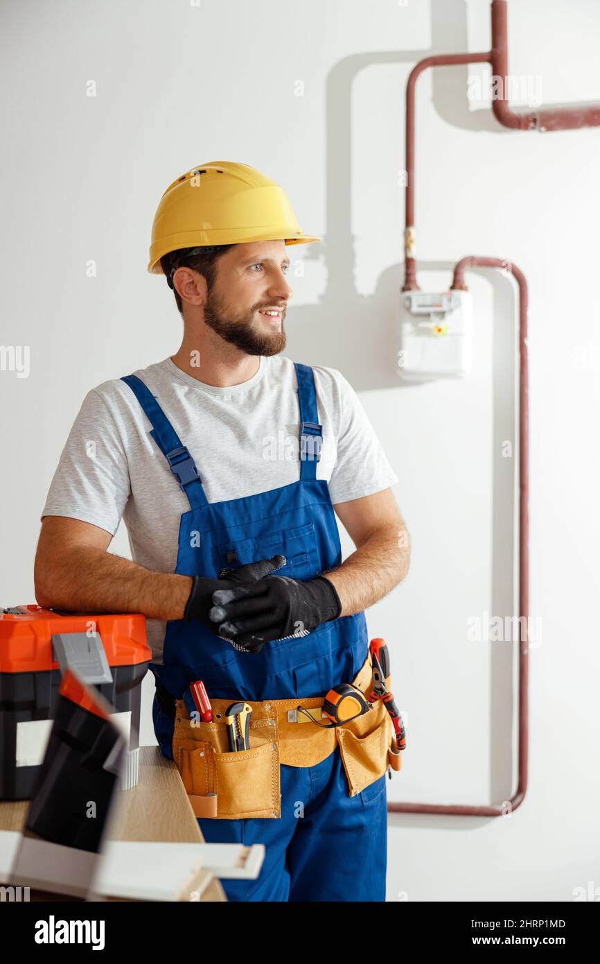 Smiling technician, handyman in uniform, hard hat and protective gloves ...