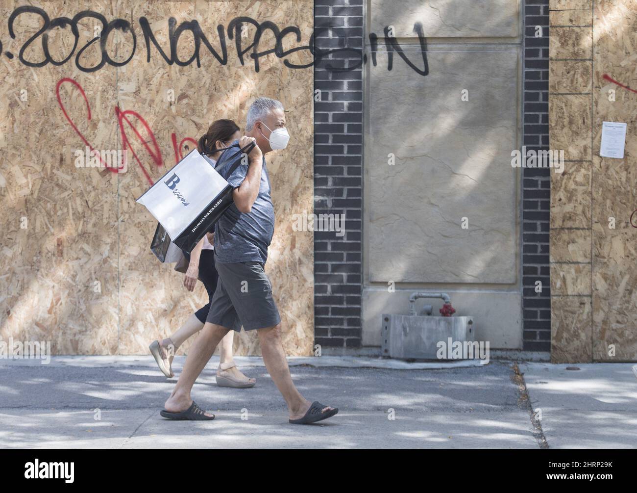 People wear face masks as they walk by a boarded up storefront in ...