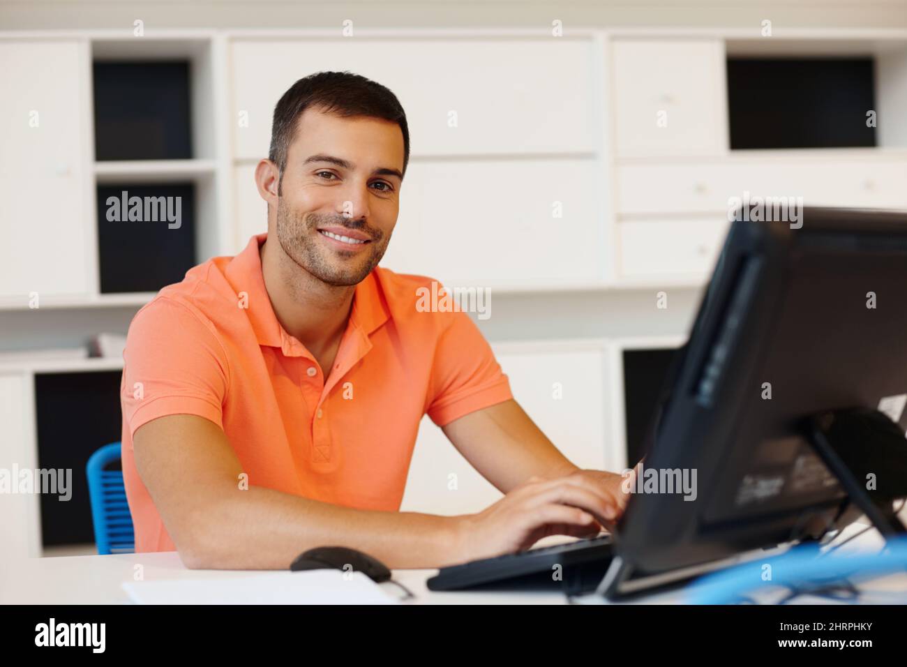 Enjoying his work. A smiling young entrepreneur working at his computer ...