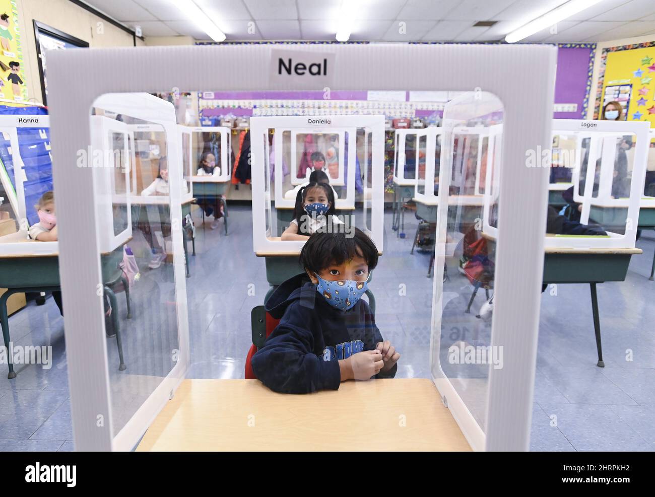 Children wearing masks sit behind screened in cubicles as they learn in ...