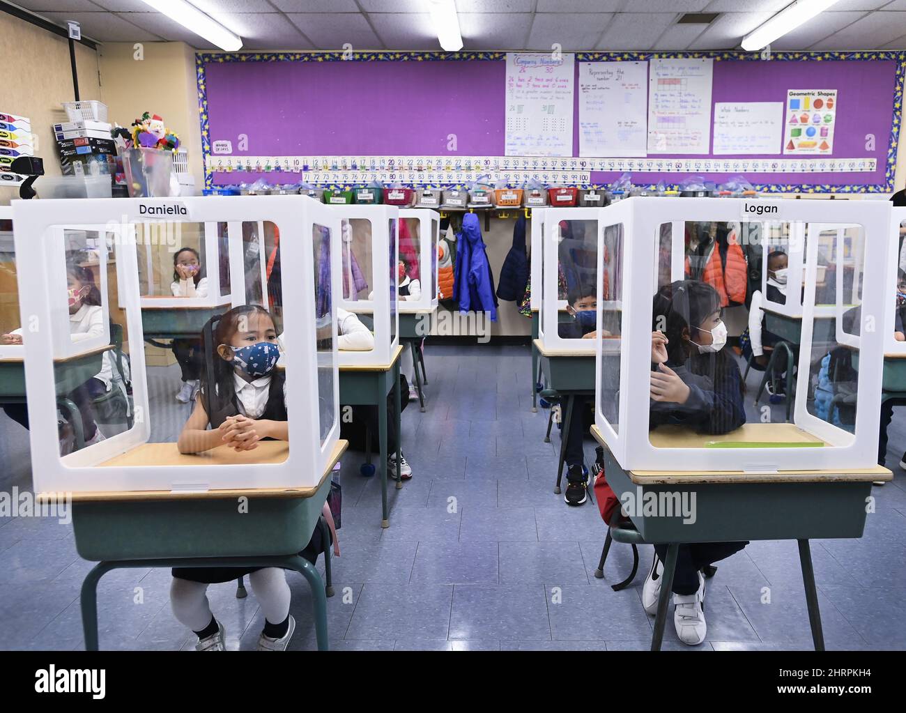 Children wearing masks sit behind screened in cubicles as they learn in ...