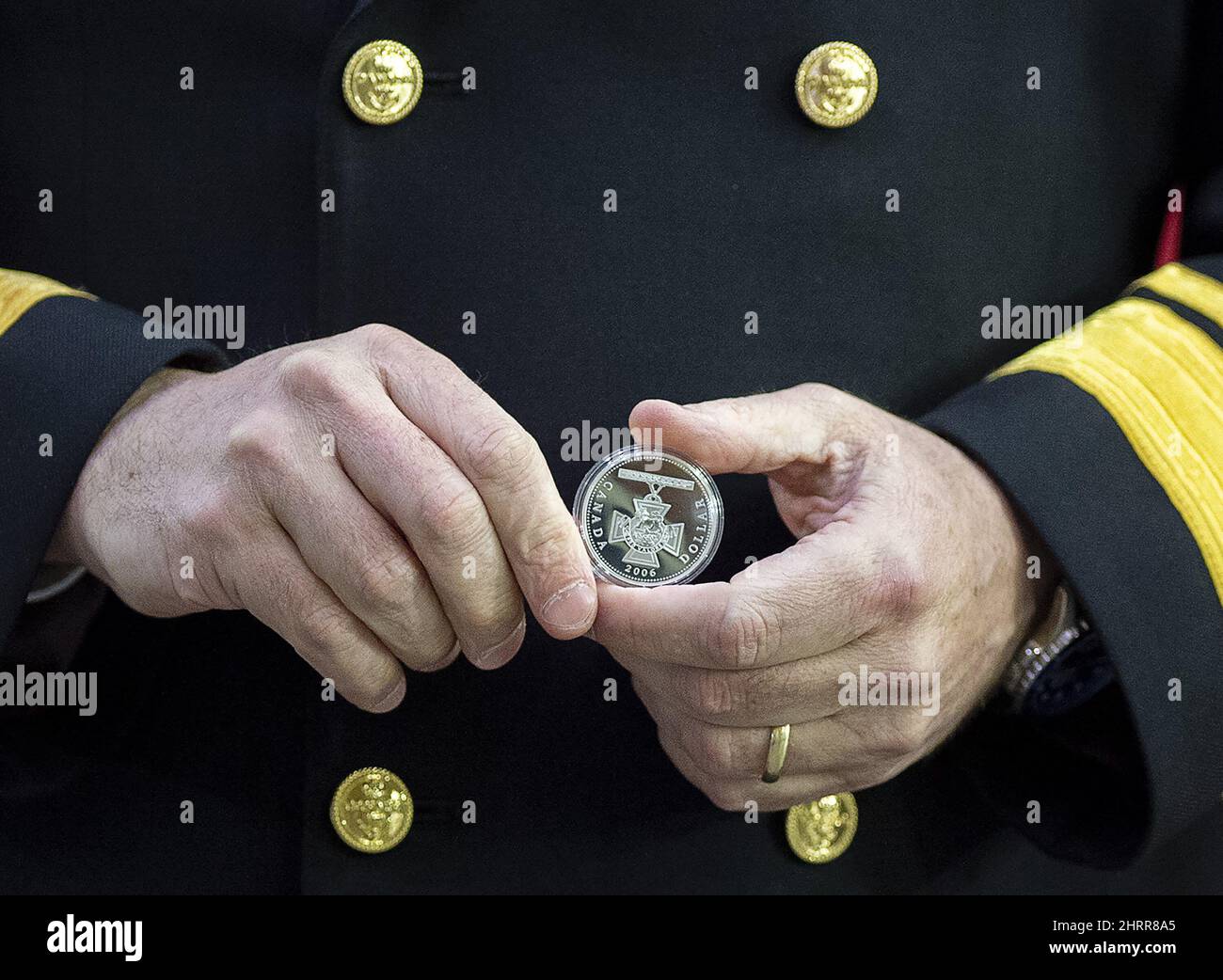 Rear Admiral Brian Santarpia holds a Canadian one dollar coin marking ...