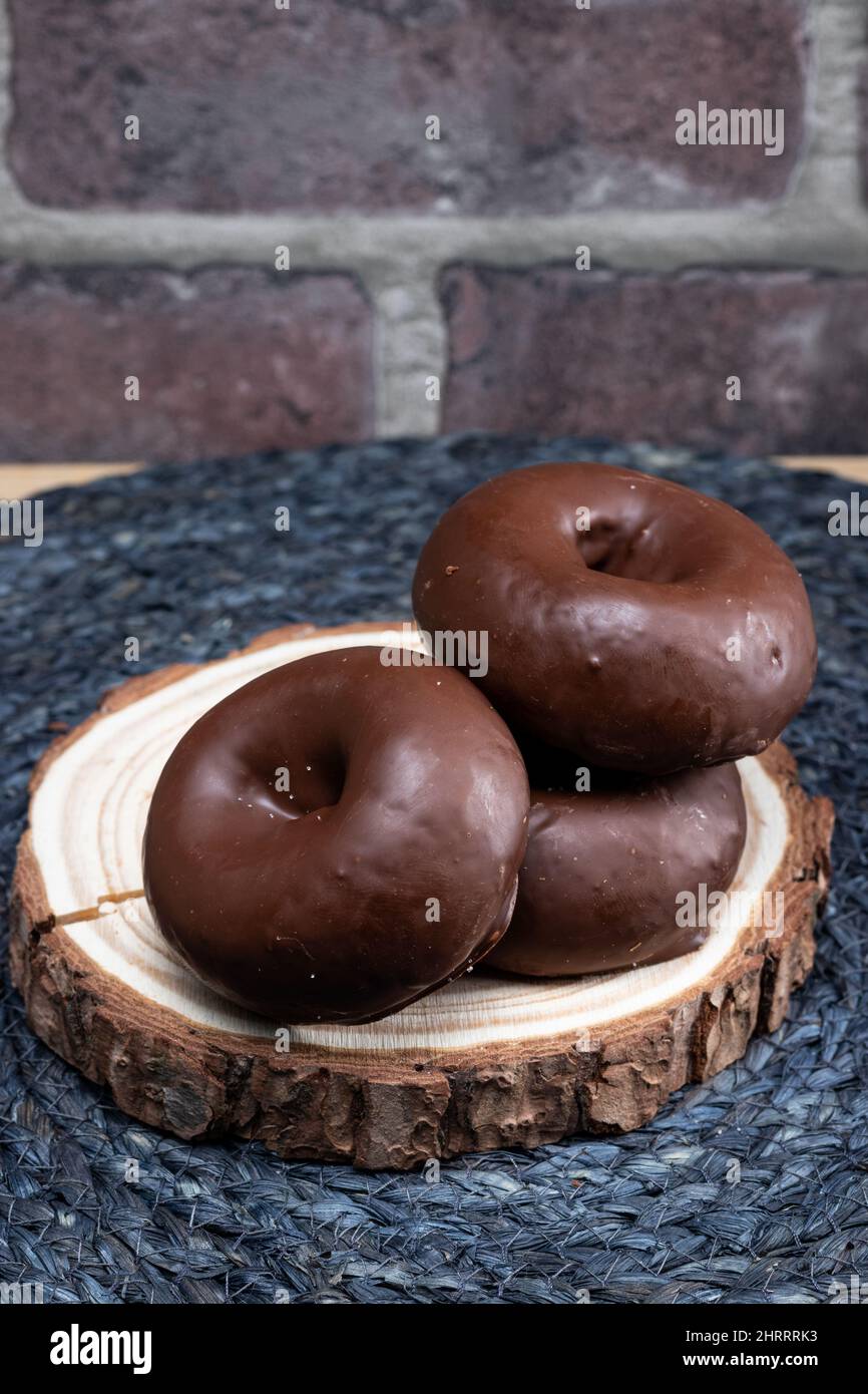 Vertical shot of a stack of chocolate-covered donuts on a wood plate ...