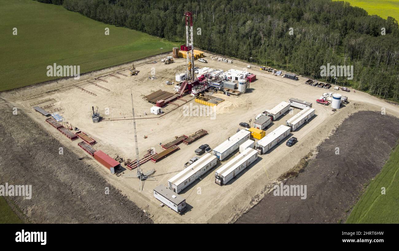 An oil drilling rig operates surrounded by canola and hay fields near ...