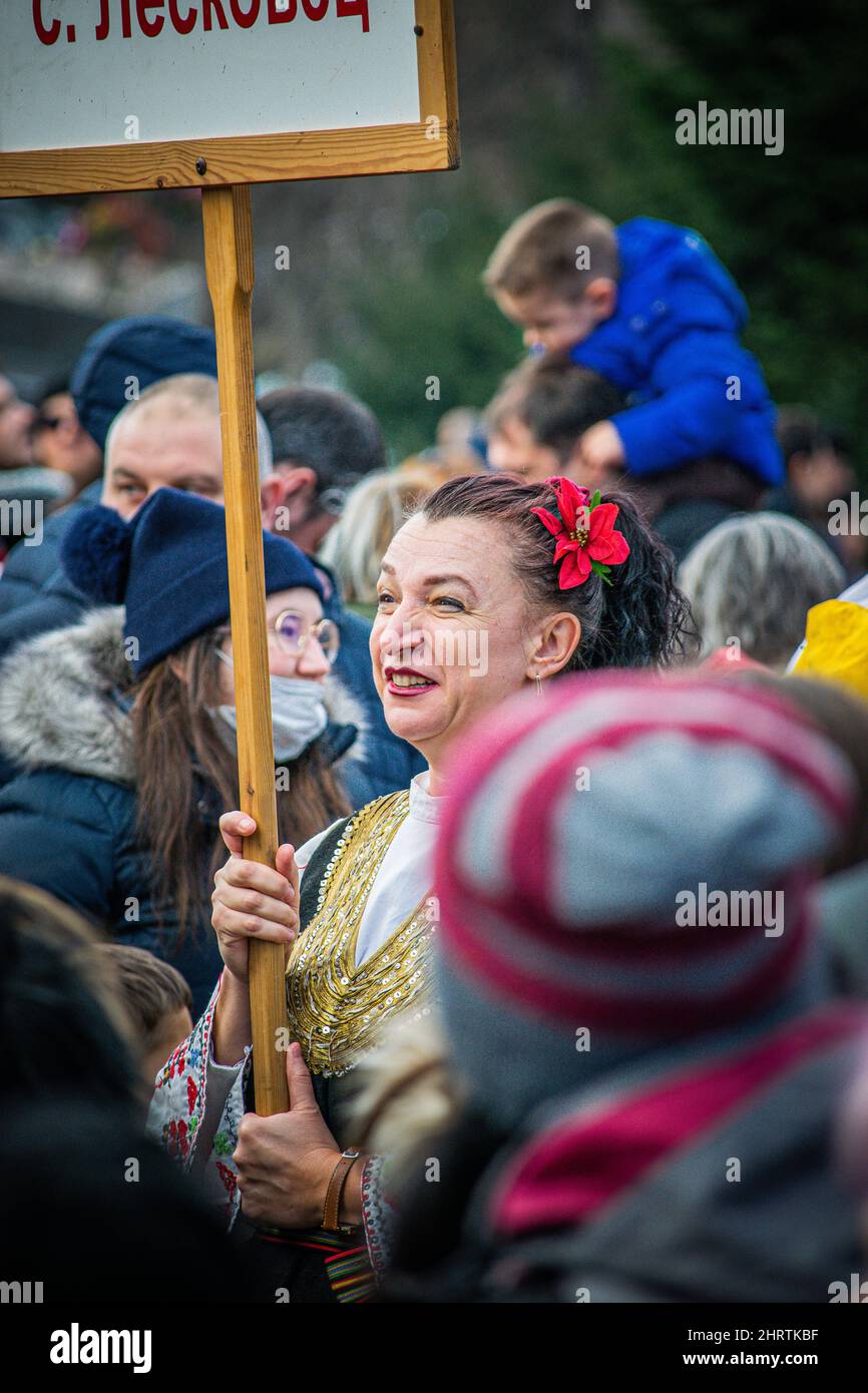 People in traditional folk costumes and masks walk on the street at the ...