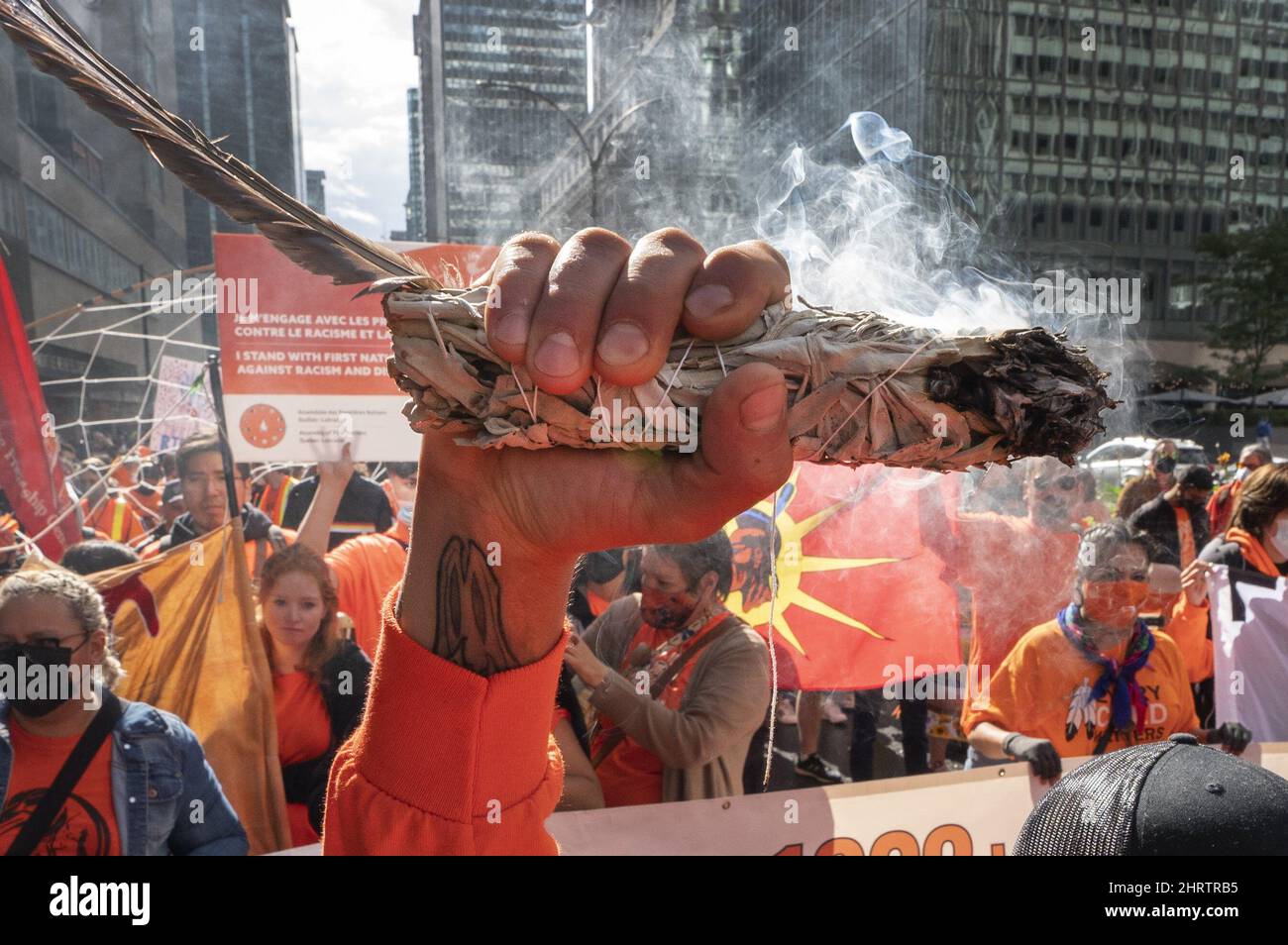 A man holds up an eagle feather and burns sweet grass as people take ...
