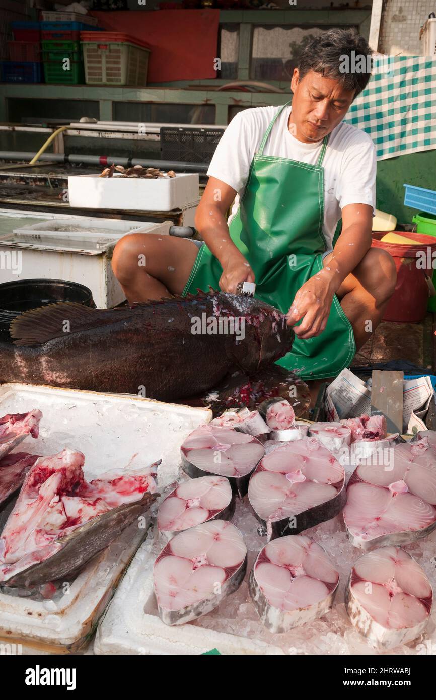 A local fishmonger cleans and cuts up a large fish at the waterfront of ...