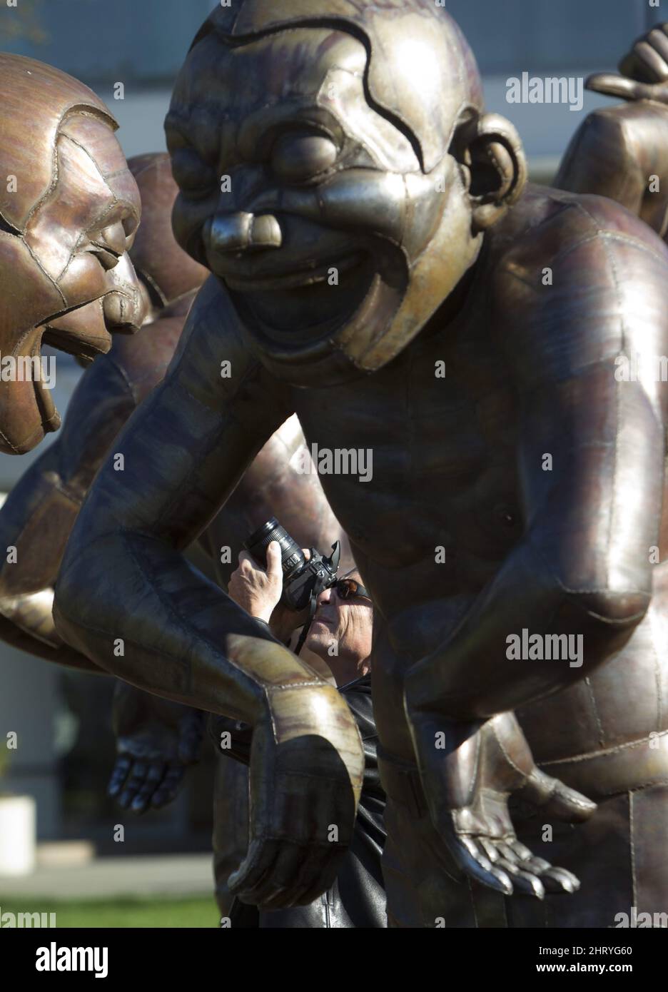 A photographer is framed by the arms of a giant bronze laughing statue ...