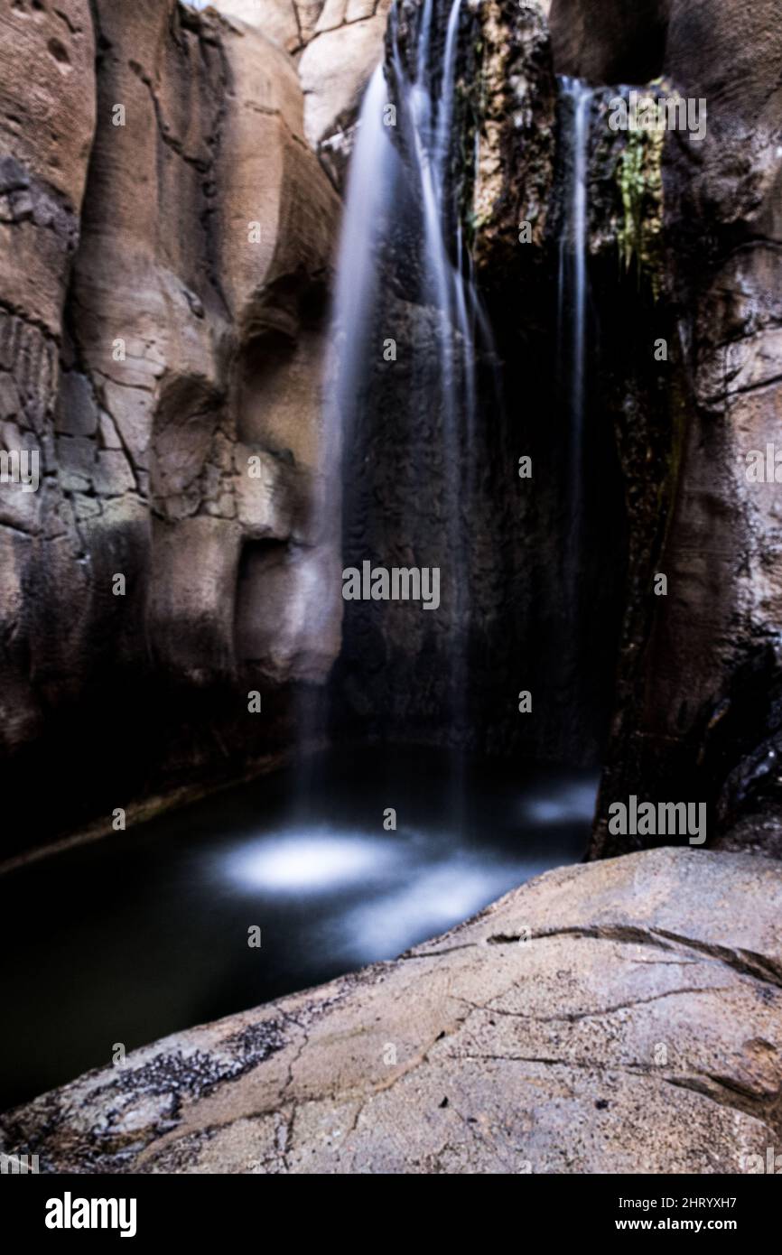 Vertical shot a waterfall with rocky walls falling on a light water ...