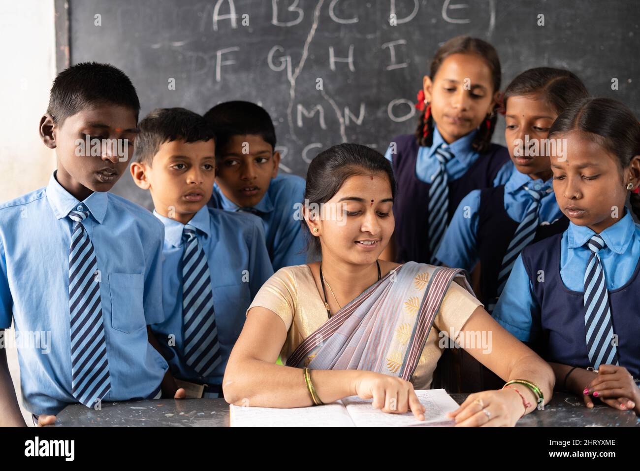 Teacher with students around explaining or teaching from book on classroom - concept of support ...