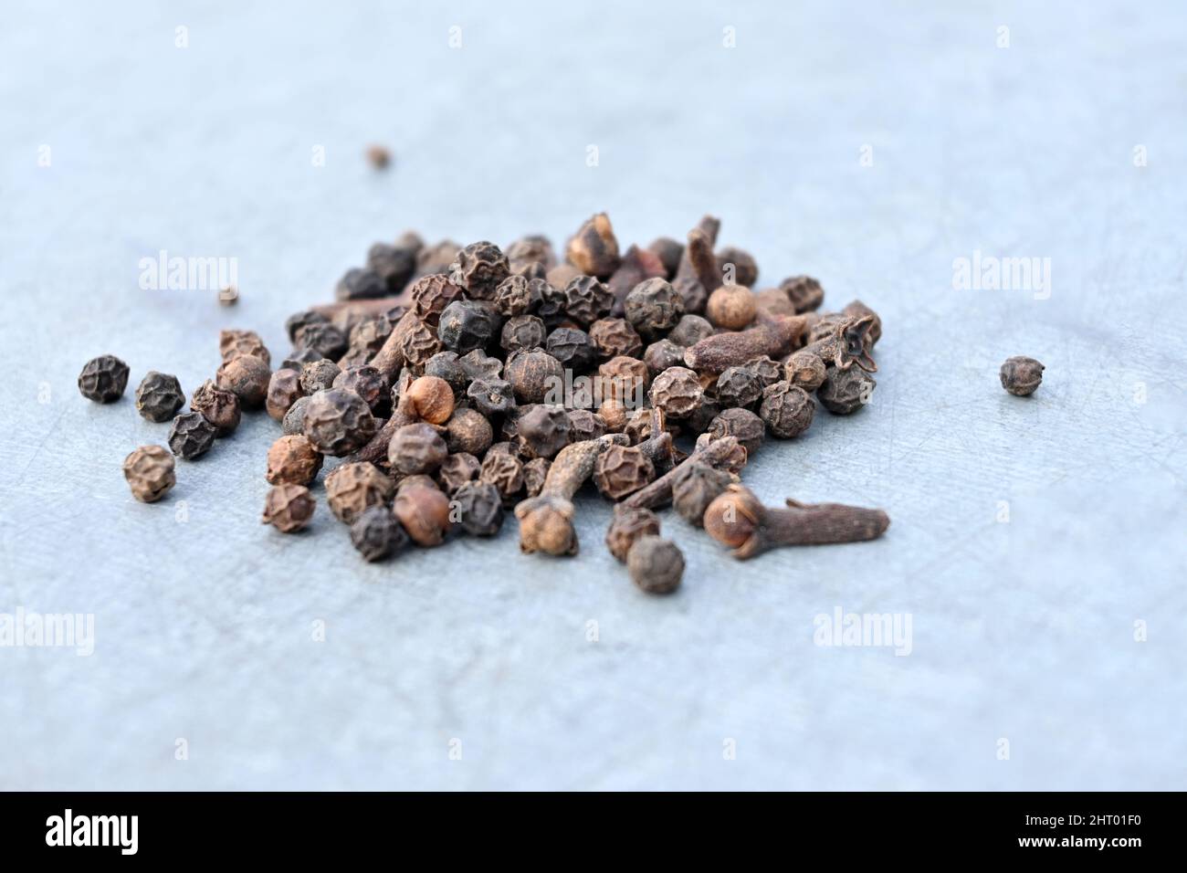 Closeup of the bunch black peppers with brown cloves over out of focus ...